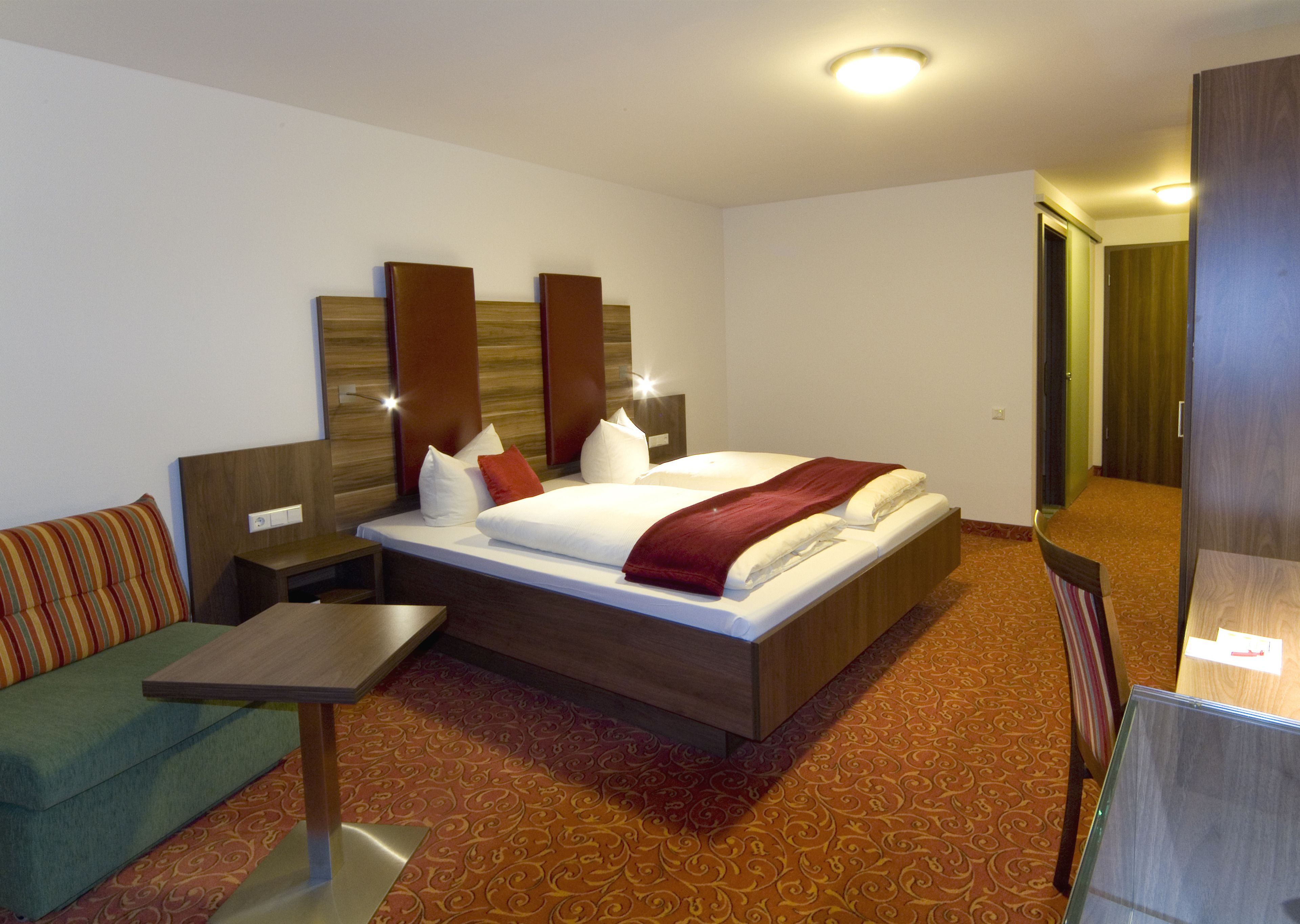 Quarto de hotel com uma cama grande, uma mesa pequena, um sofá e um espelho.