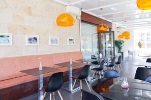 Restaurante moderno com parede de mármore, luminárias pendentes laranja, cadeiras pretas e um banco estofado vermelho.