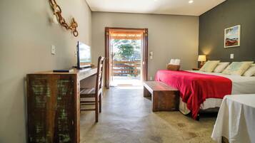 Quarto com cama, escrivaninha e computador. Tem uma janela com vista para árvores e uma porta que dá para o exterior.