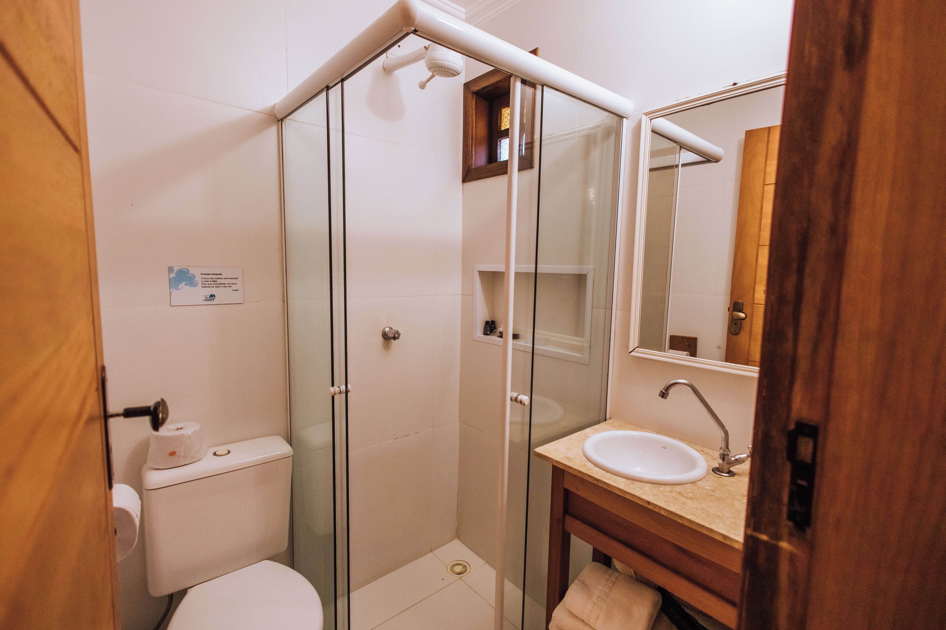 Casa de banho compacta com cabine de duche em vidro, sanita e lavatório com espelho acima.