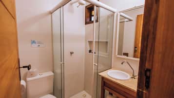 Casa de banho compacta com cabine de duche em vidro, sanita e lavatório com espelho acima.