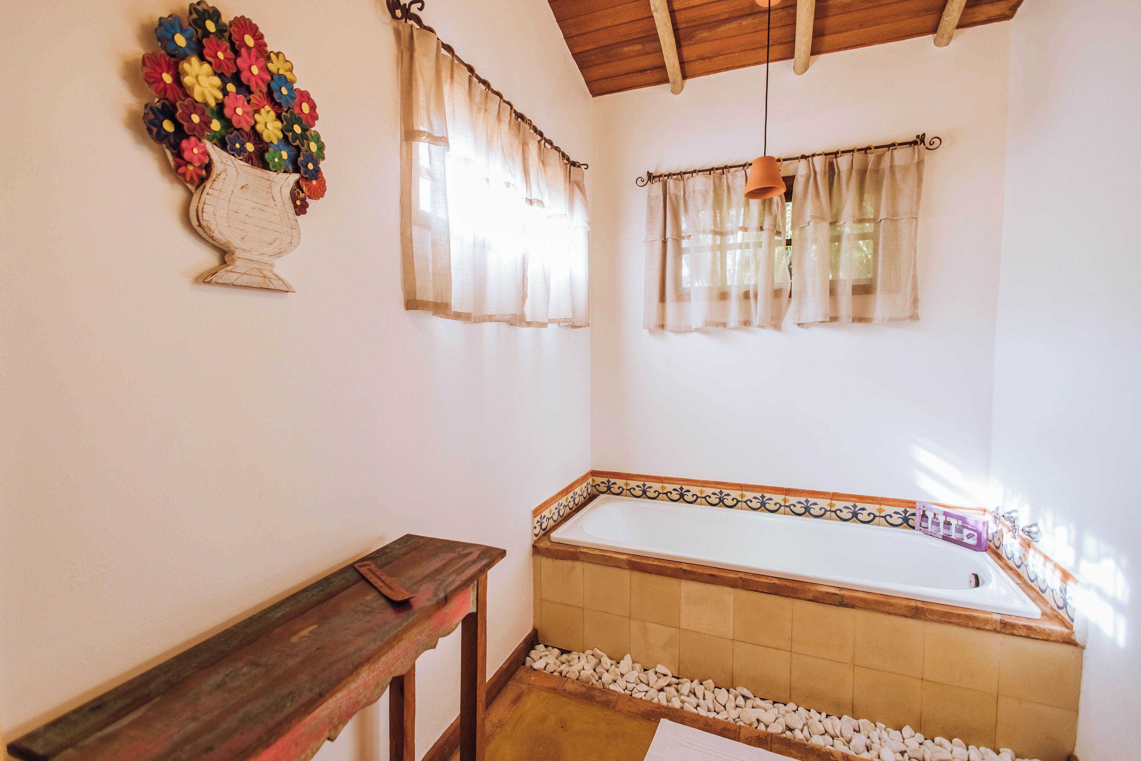 Um banheiro com banheira, um banco de madeira e um vaso decorativo com flores.