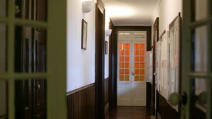Um corredor com lambris de madeira, uma porta com painéis de vidro em tom alaranjado e um luminário na parede.