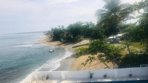 Vista da piscina com vista para a praia, cadeiras de sol e um pequeno barco.