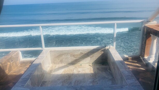 Vista de uma varanda com barreira de vidro, com vista para o oceano e ondas quebrando na costa.