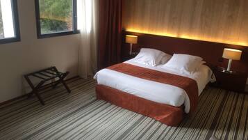 Quarto de hotel com uma cama grande, duas luminárias de cabeceira, um painel de cabeceira de madeira, um tapete listrado e uma janela com cortinas.