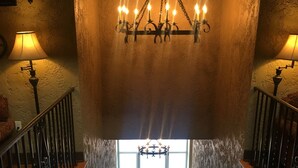 Uma escadaria imponente com um candelabro, um tapete estampado e vista para o exterior.