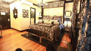 Um quarto com uma cama grande, um banquinho, um candelabro e uma porta.