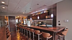 Uma área de bar com um balcão comprido e vários bancos, uma geladeira e uma variedade de garrafas nas prateleiras.