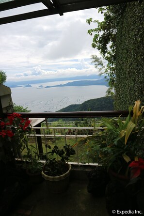 Varanda com vista para uma grande extensão de água e ilhas distantes, rodeada por vasos de plantas e uma grade de metal.