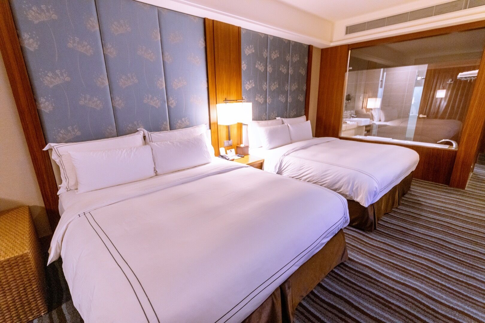 Quarto de hotel com duas camas, um espelho grande e uma cabeceira de madeira.