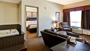 Quarto de hotel com banheiro, uma cama, um sofá, uma mesa com telefone e uma janela com cortinas.