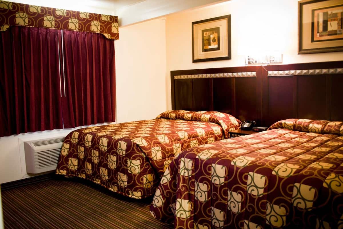 Quarto de hotel com duas camas, uma janela grande com cortinas, ar condicionado fixado na parede e quadros decorativos sobre as camas.