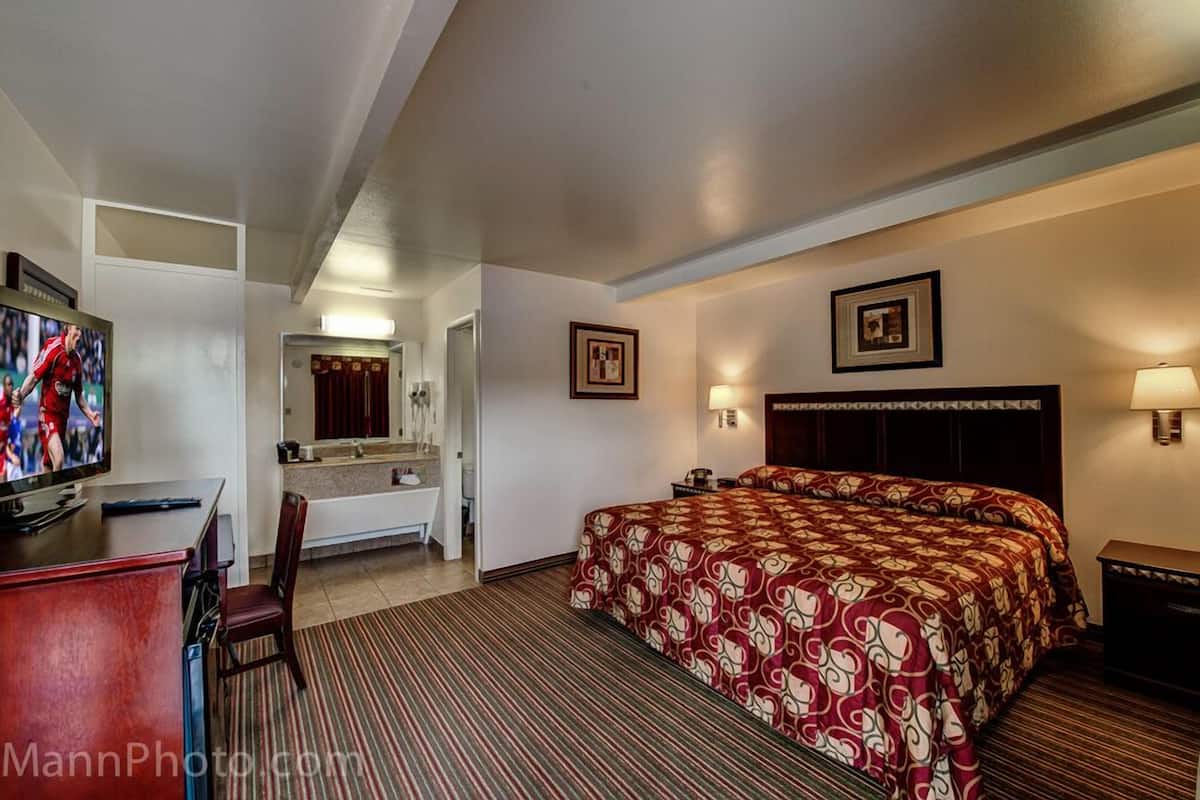 Quarto de hotel com uma cama grande, uma mesa de escritório com televisão, banheiro e mesa de cabeceira.
