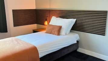 Quarto de hotel com cama, mesa de cabeceira, pintura de pôr do sol e carpete escuro.