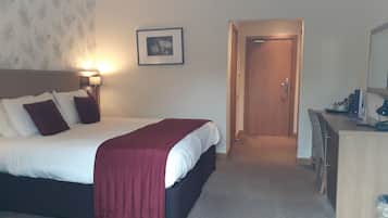 Quarto de hotel com cama, mesa de cabeceira, abajur e porta que dá para outro aposento.