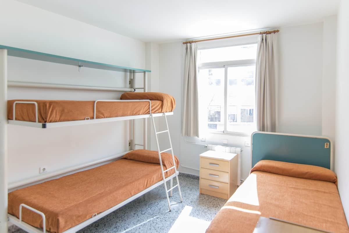 Quarto de dormitório com beliches, uma escrivaninha e uma janela com cortinas.