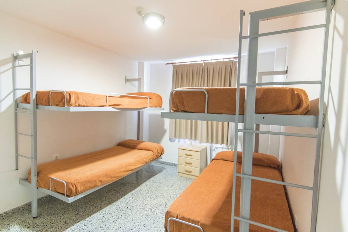 Quarto de dormitório com beliches, uma cômoda pequena e uma janela com cortinas.