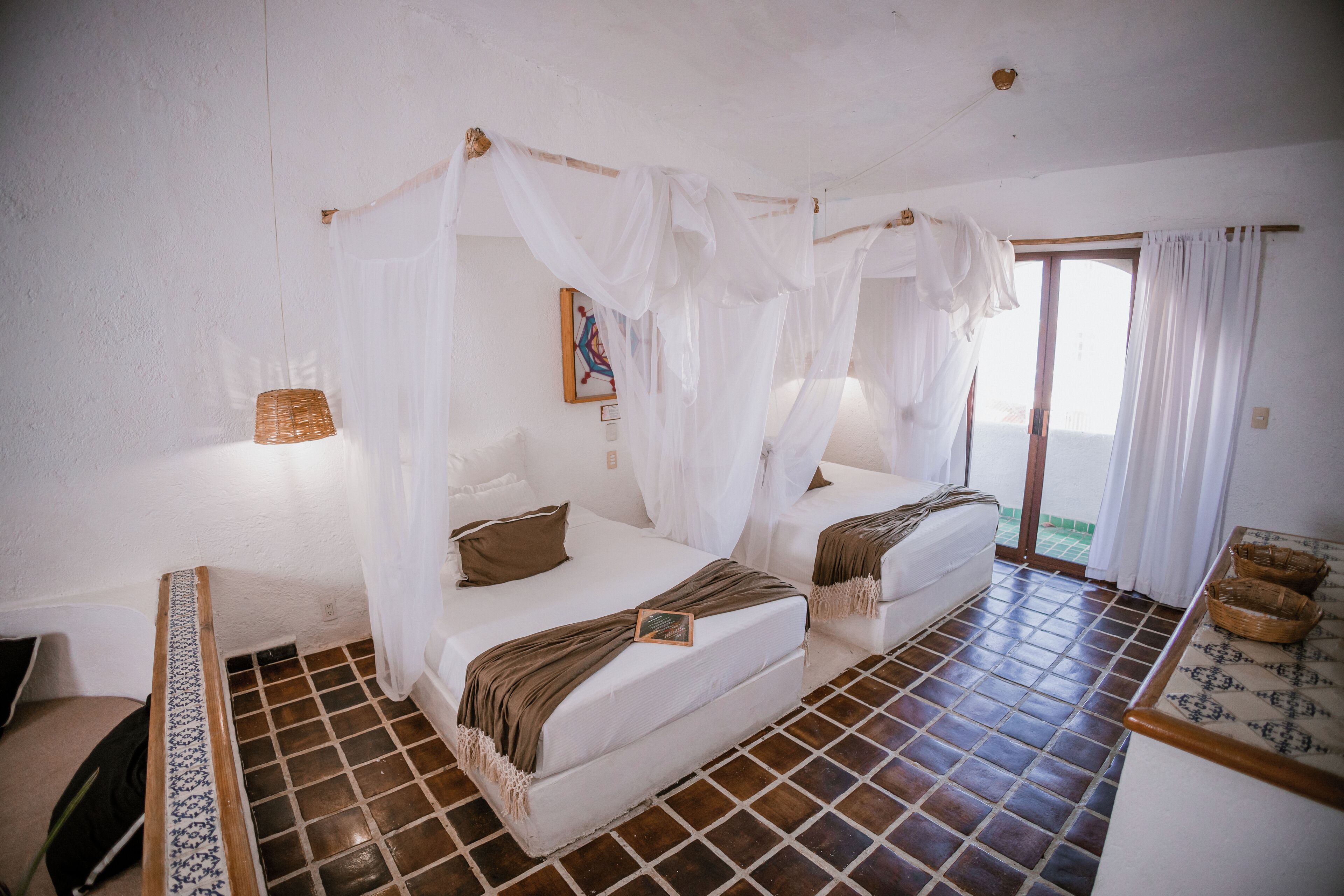 Quarto com duas camas, uma janela grande e piso em azulejos.