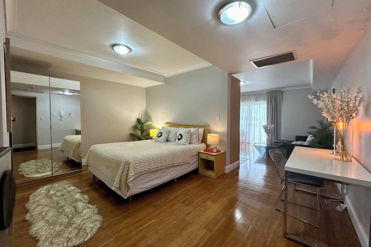 Quarto moderno com cama, mesa de cabeceira, abajur e espelho.
