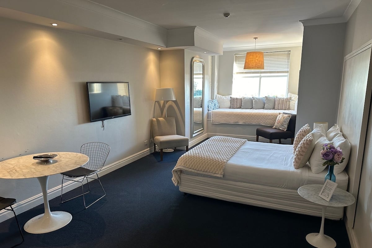 Quarto de hotel com cama, televisão, escrivaninha e cadeira.