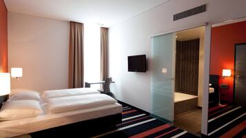 Quarto de hotel com cama, escrivaninha, televisão e banheiro.