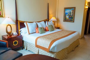 Quarto de hotel com uma cama grande, duas mesas de cabeceira com luminárias, um quadro na parede e um relógio em uma das mesas.