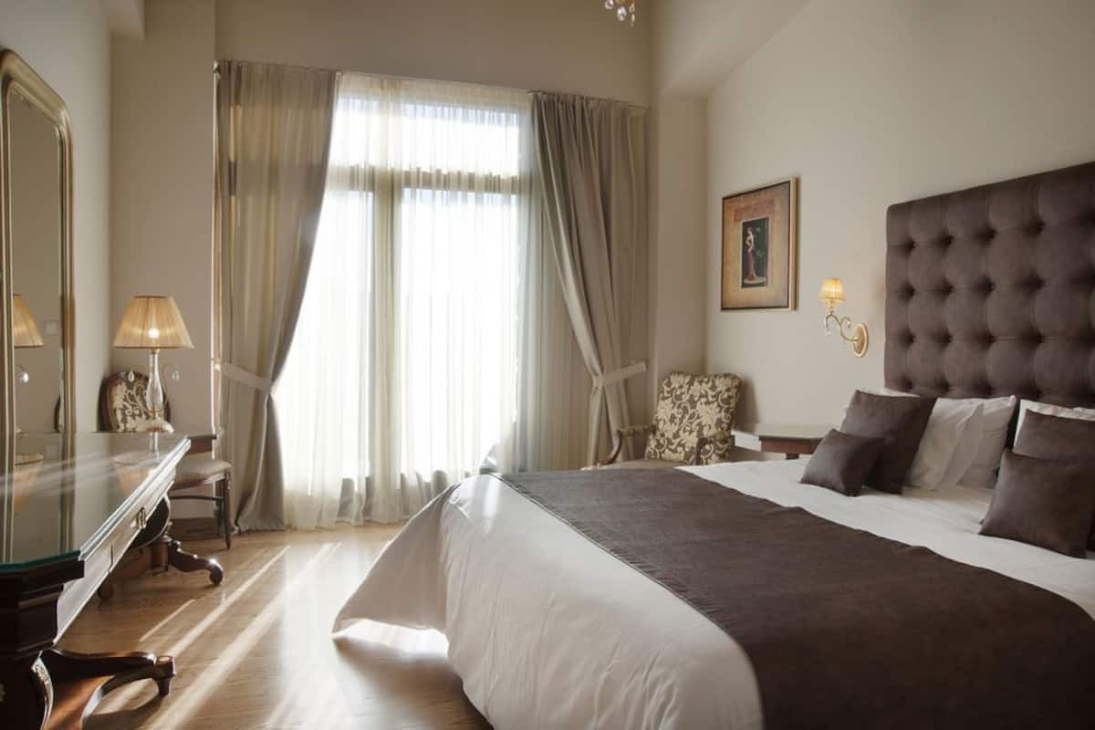 Quarto de hotel com uma cama grande, uma escrivaninha, uma cadeira e uma janela com cortinas.