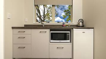 Cozinha compacta com micro-ondas integrado, chaleira e janela com vista para árvores e céu.