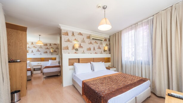 Quarto de hotel com cama, mesas de cabeceira, escrivaninha e janela com cortinas.