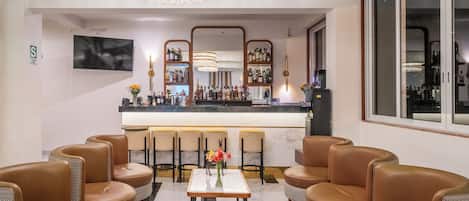 Uma área de bar com poltronas de couro, uma mesa com tampo de mármore e um candelabro.