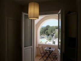 Varanda com vista para uma piscina e árvores, uma mesa e cadeira de madeira, e um lustre suspenso.