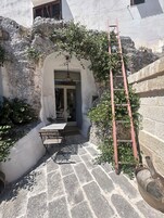 Um pátio de pedra com bancos de madeira, uma escada e um vaso de planta.