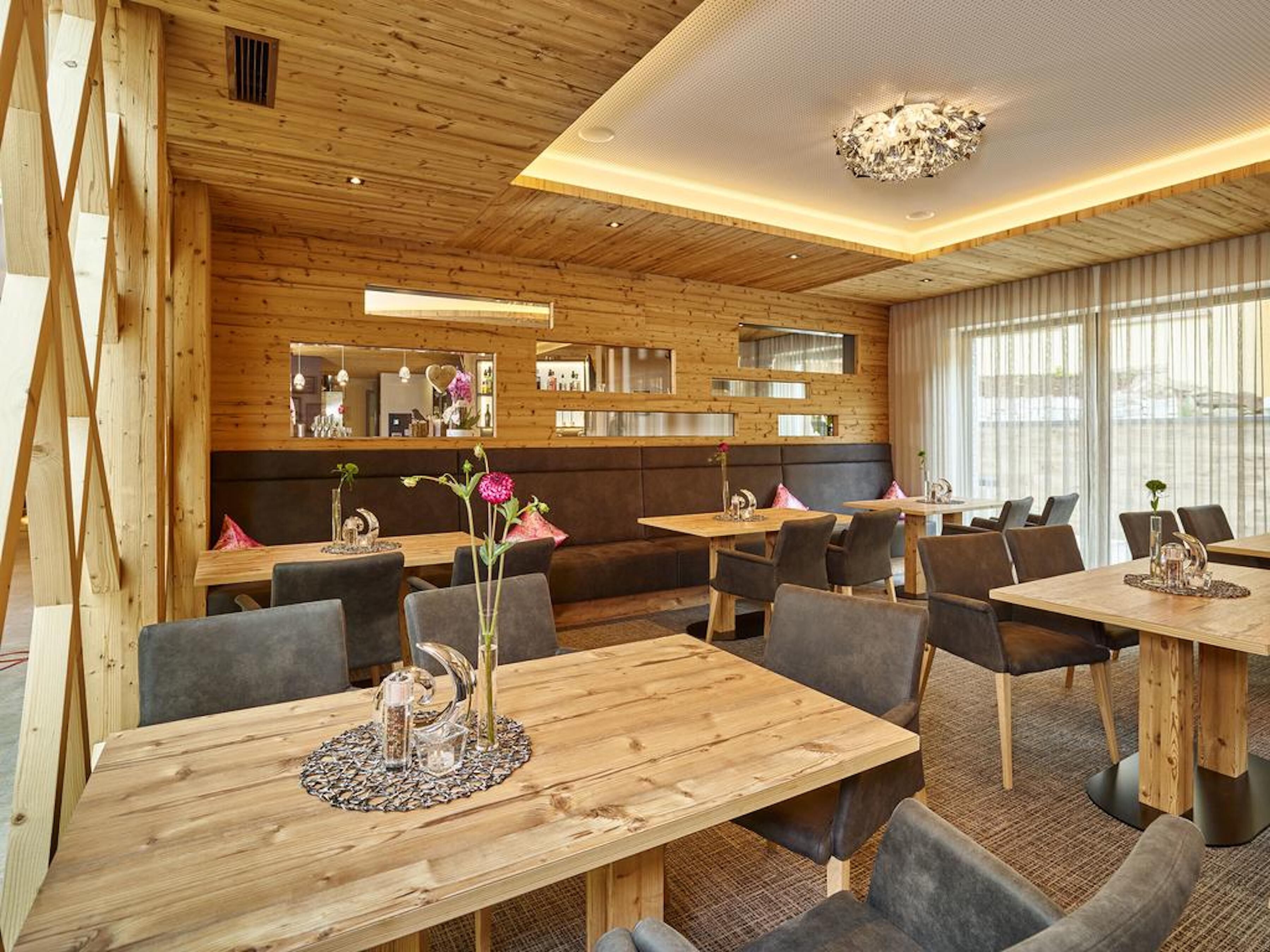 Restaurante moderno com paredes e teto de madeira, apresentando várias mesas e cabines.
