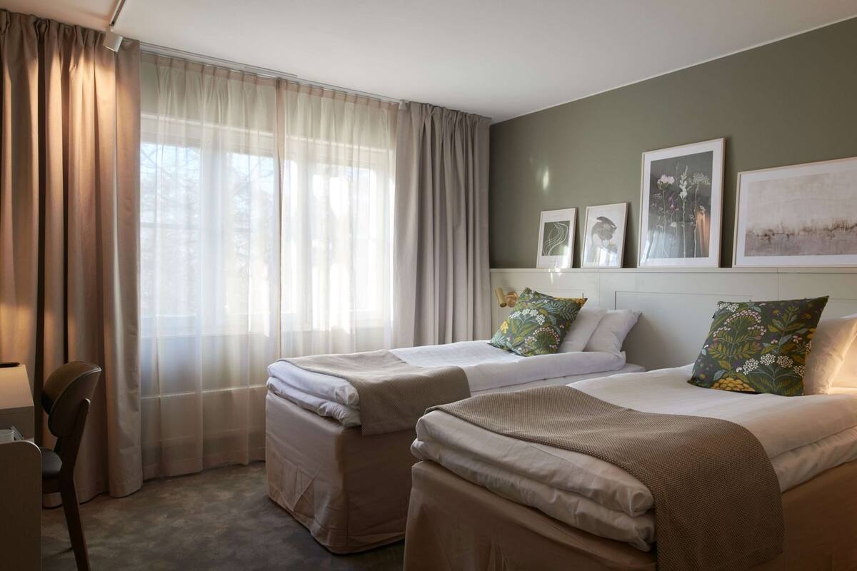 Quarto de hotel com duas camas, uma escrivaninha e uma cadeira.