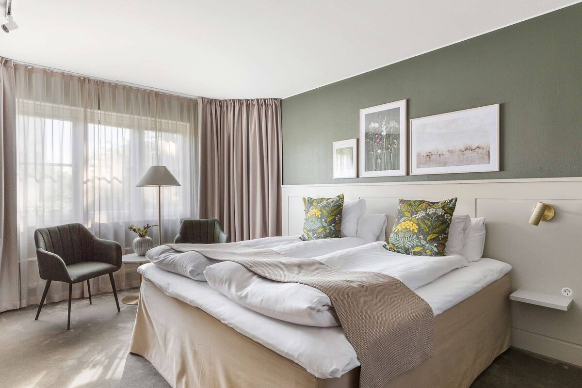 Quarto de hotel com uma cama grande, uma cadeira, um abajur e obras de arte na parede.
