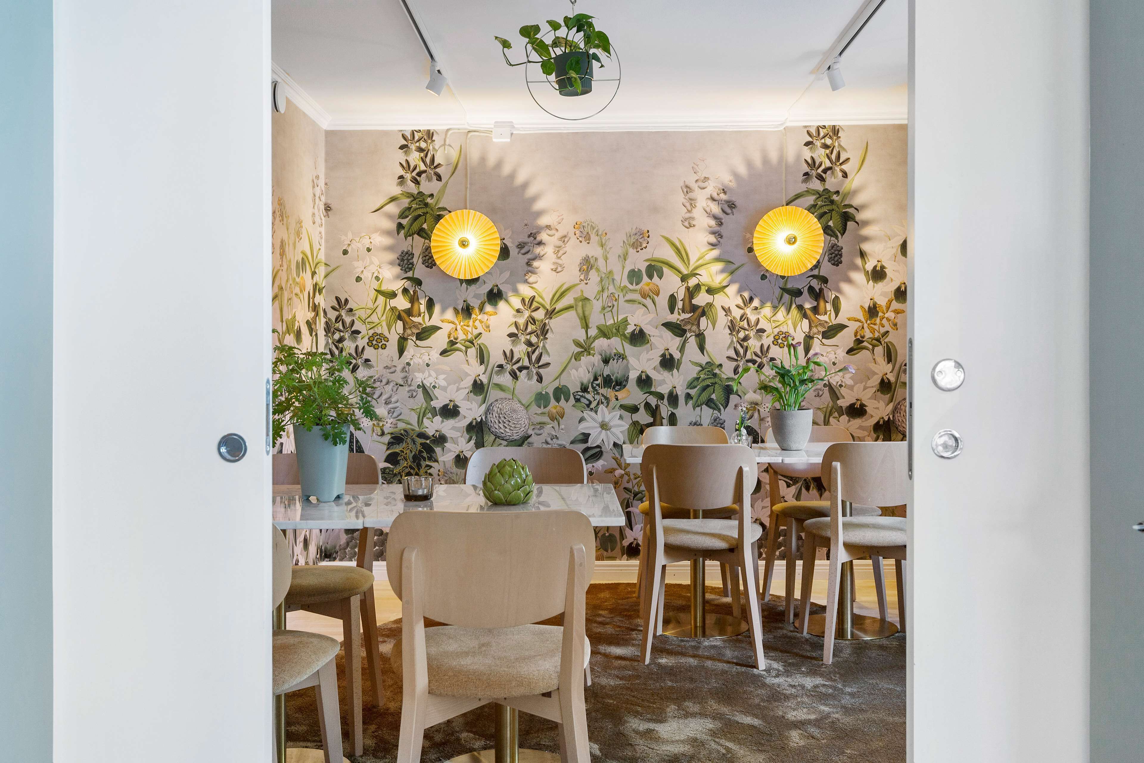 Uma sala de jantar com papel de parede floral, duas luminárias pendentes e uma mesa com cadeiras.