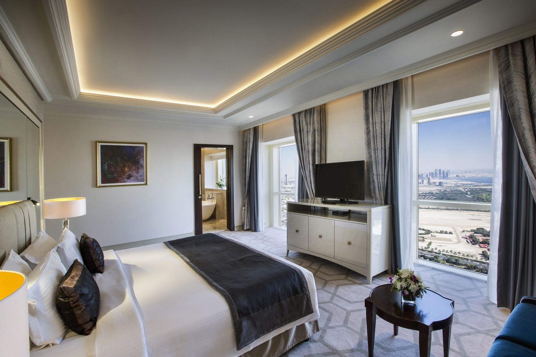Quarto de hotel moderno com uma cama grande, uma TV, uma escrivaninha e vista para a cidade.