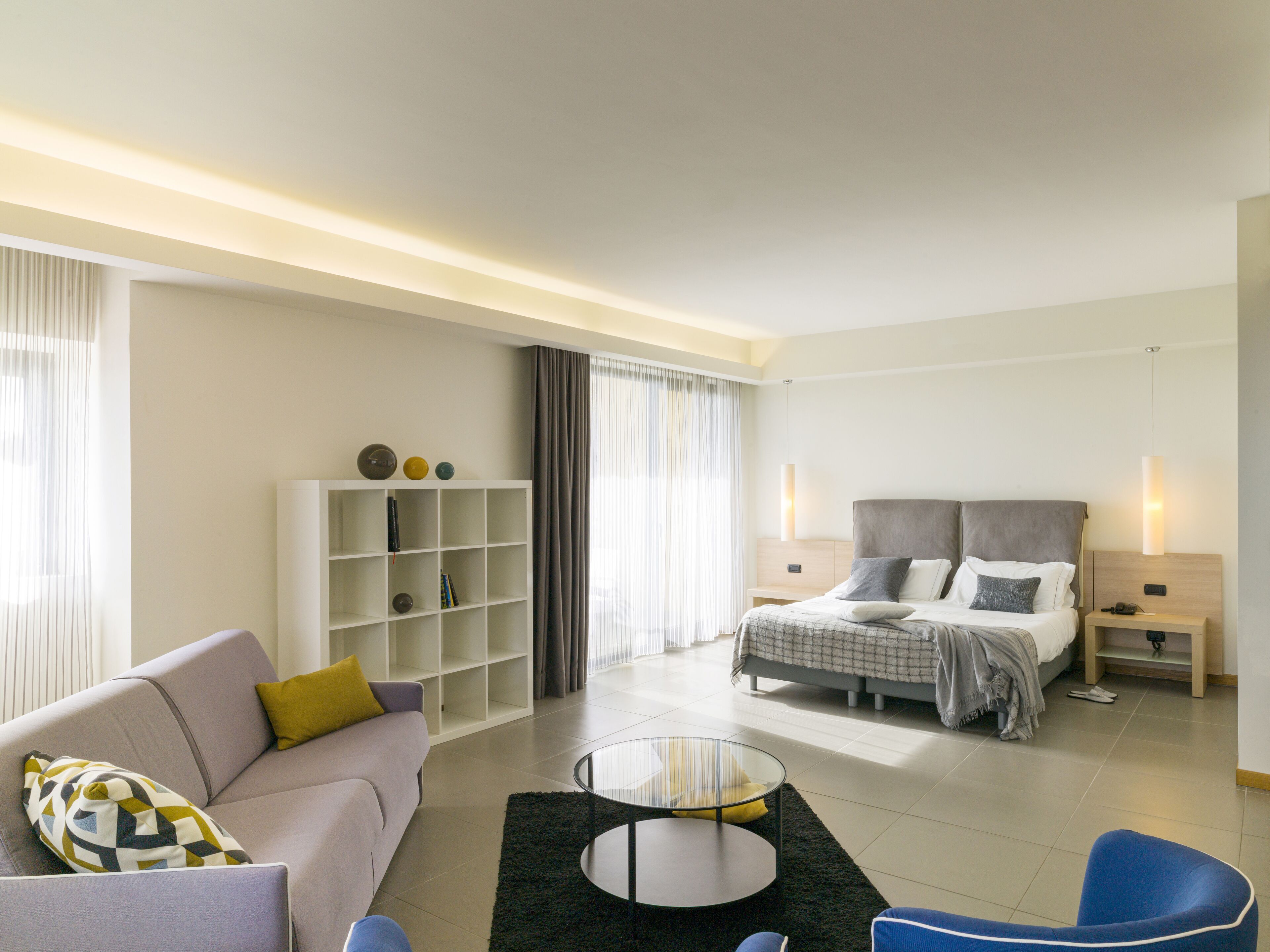 Quarto de hotel moderno com uma cama, um sofá, uma mesa de centro e uma estante.