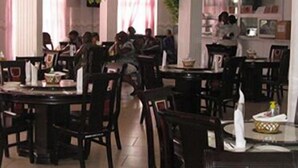 Um restaurante com várias mesas e cadeiras redondas, algumas com guardanapos e acompanhamentos.