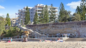 Um hotel à beira-mar, com vários andares, uma escadaria que dá para a praia e vista para o mar.