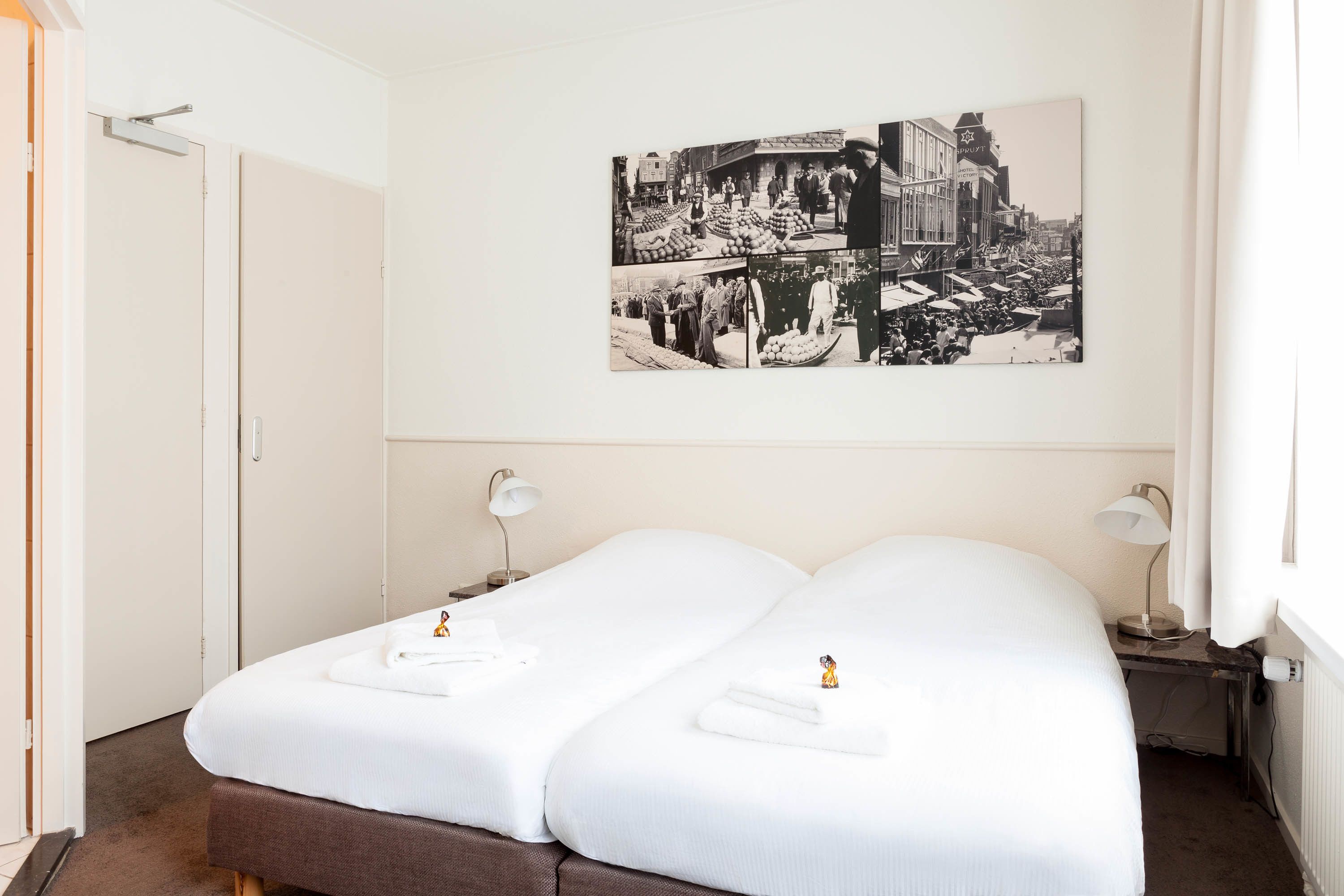 Quarto de hotel com duas camas, um quadro na parede, abajures e uma porta.