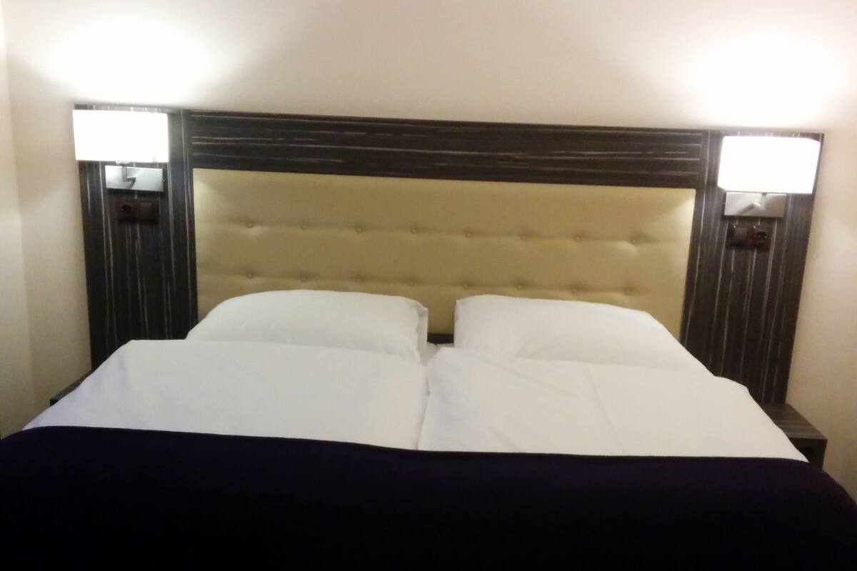 Quarto de hotel com uma cama grande, duas luminárias de cabeceira e cabeceira com design acolchoado.