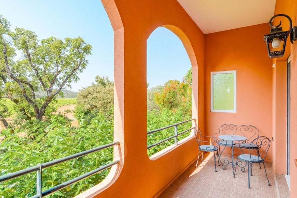 Uma varanda com vista para um vinhedo, uma mesa com cadeiras e um abajur fixado na parede.