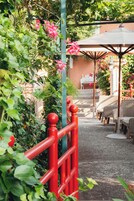 Caminho no jardim que leva a um espaço de estar ao ar livre, com guarda-corrimão vermelho e vegetação.
