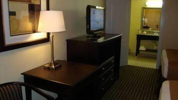 Quarto de hotel com escrivaninha, cadeira, televisão, cama e banheiro visível através de uma porta aberta.