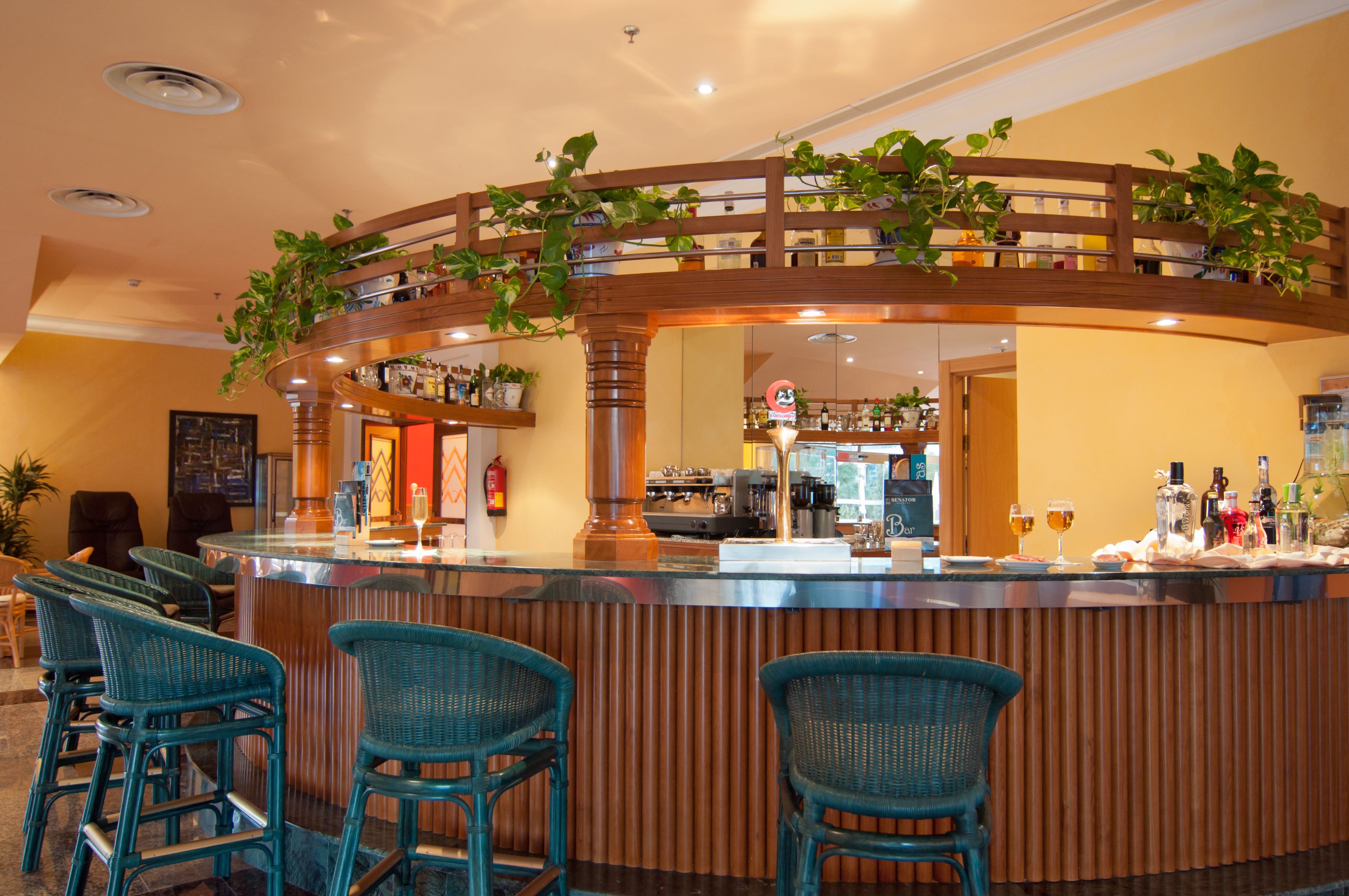 Uma área de bar com balaústres de madeira, plantas verdes e banquetas.