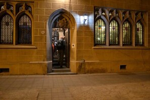 Entrada de um edifício com fachada de pedra, porta em arco e janelas com vitrais.
