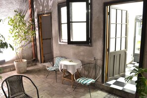 Uma área de pátio com mesa e cadeiras, um vaso de planta e piso xadrez.