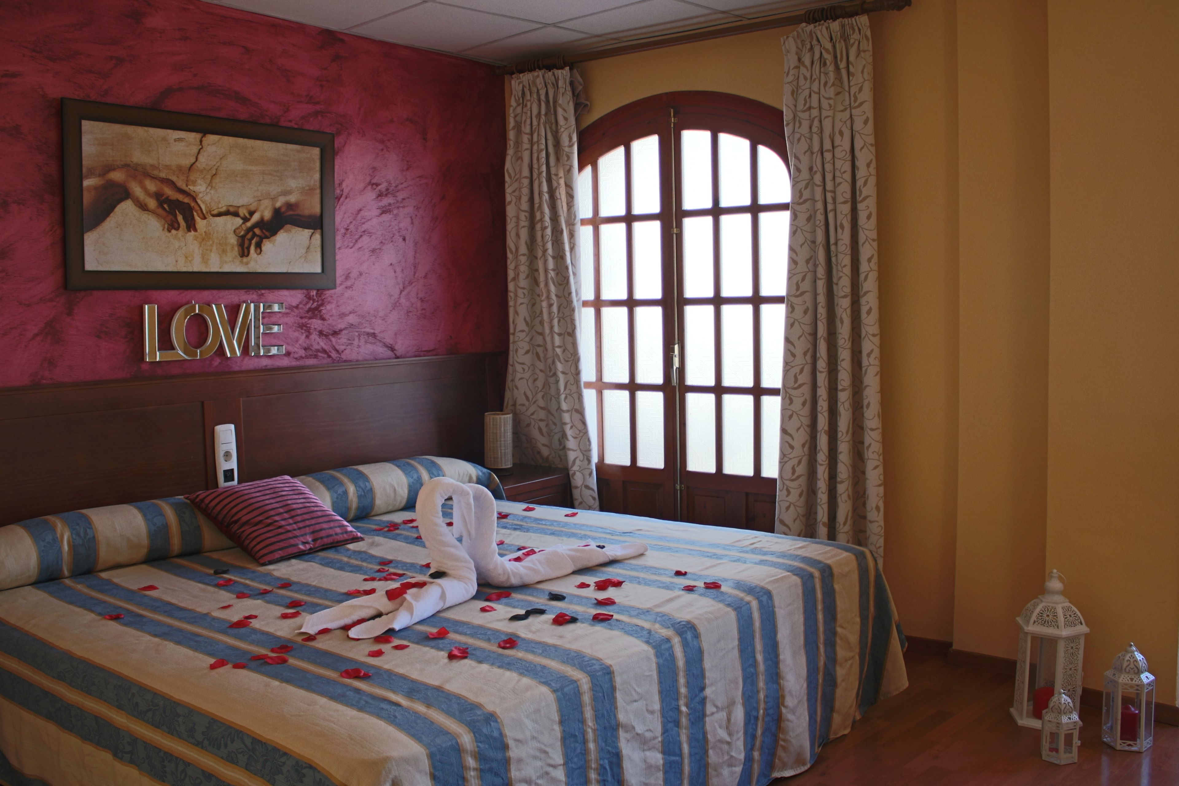 Quarto de hotel com uma cama, um quadro na parede e uma janela com cortinas.